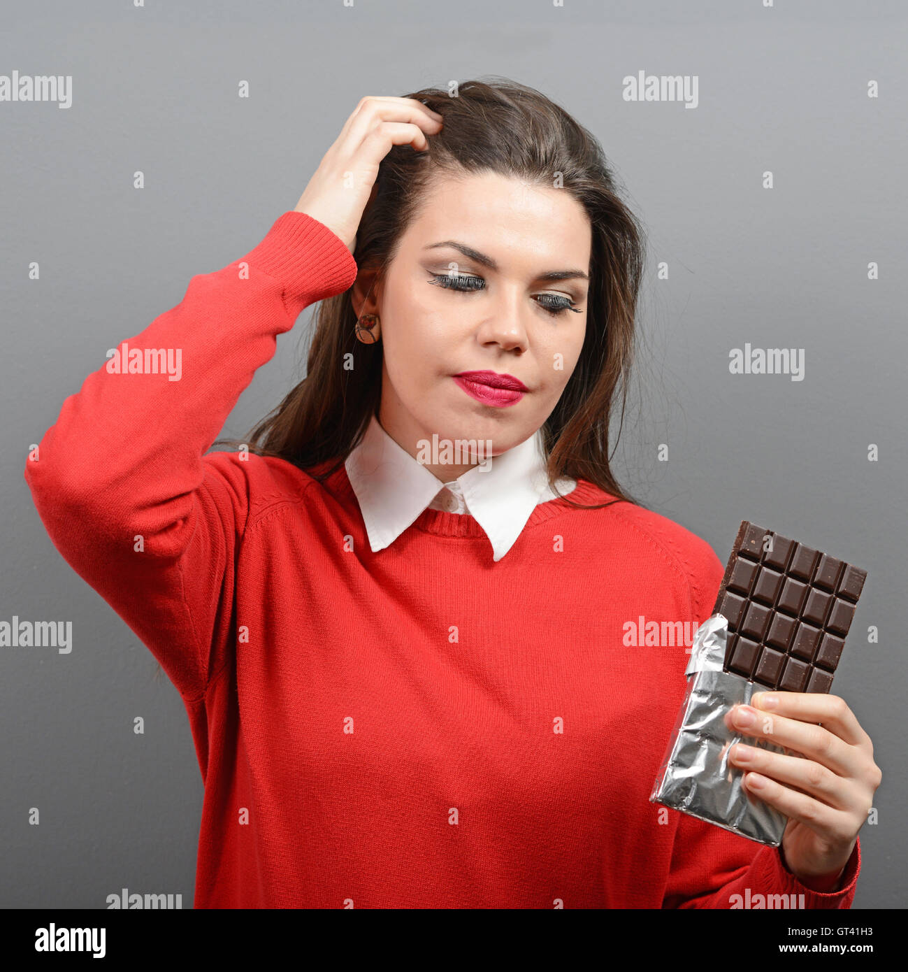 Beautiful woman in temptation of eaiting a chocolate against gray ...