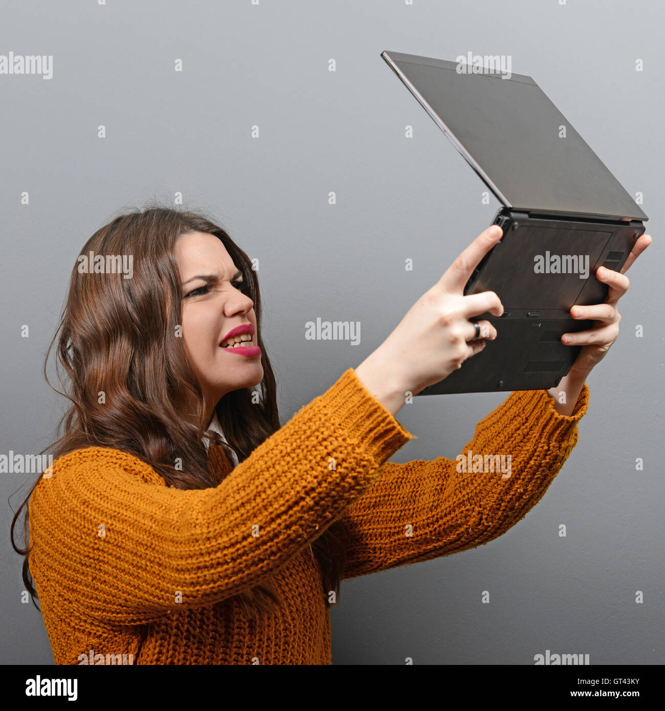 Portrait of angry woman screaming at her laptop against gray background ...