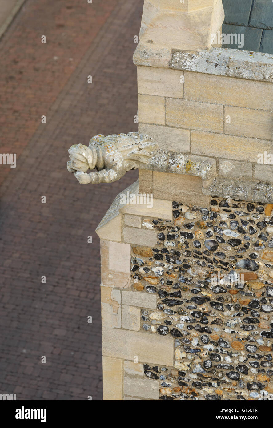 Carved gargoyle rain water spout built into corner of flint and stone ...