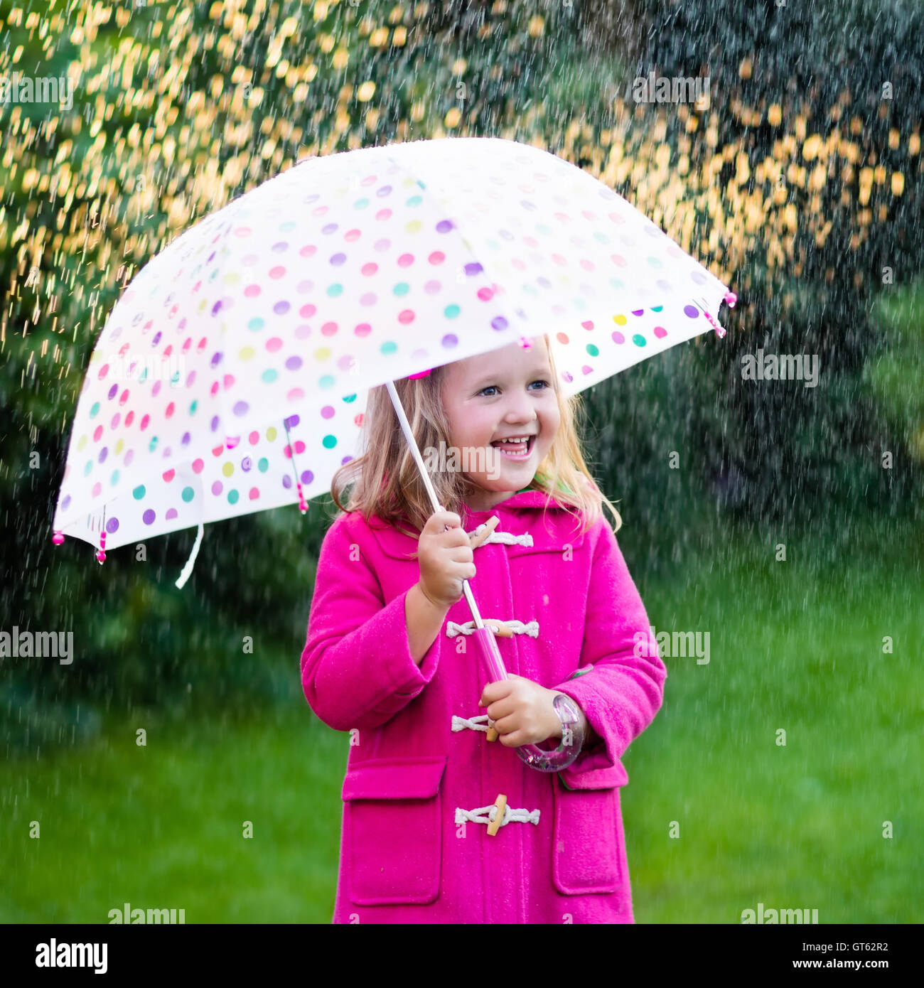 Little girl playing in rainy summer park. Child with colorful rainbow ...