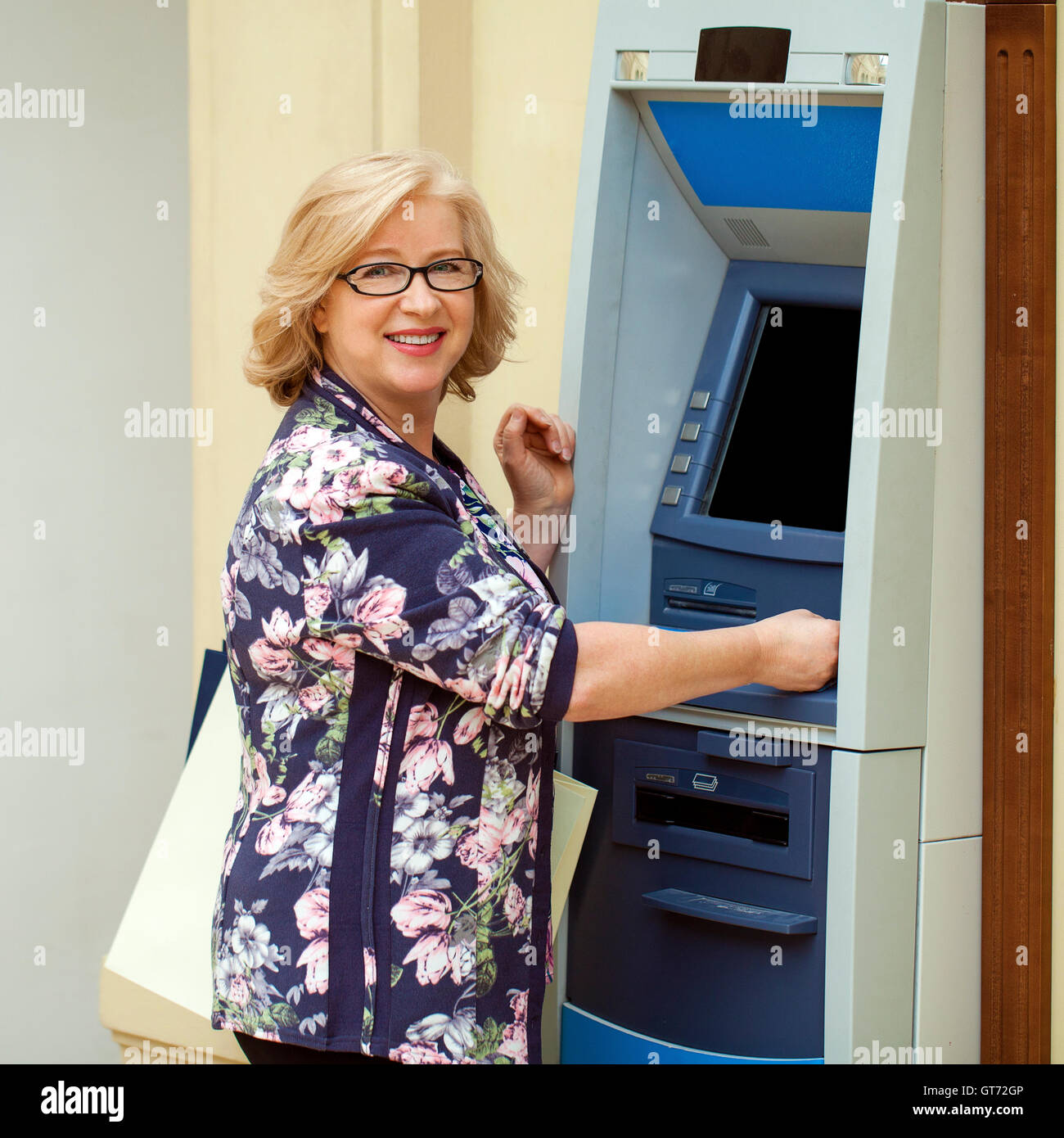 Mature blonde woman with credit card in hand near automated teller ...