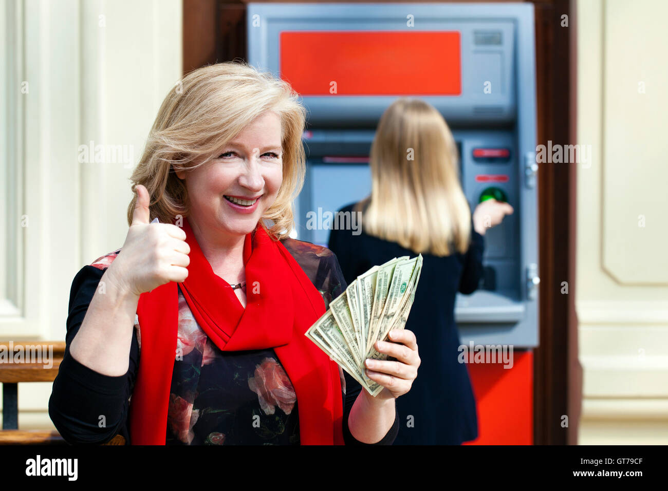 Mature blonde woman counting money near automated teller machine in ...