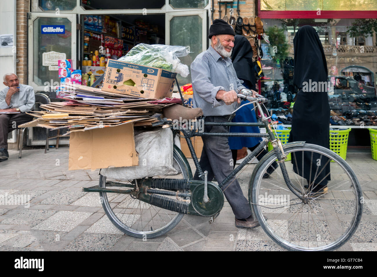 A happy man rolling a bicycle loaded with cardboard and vegetables down ...