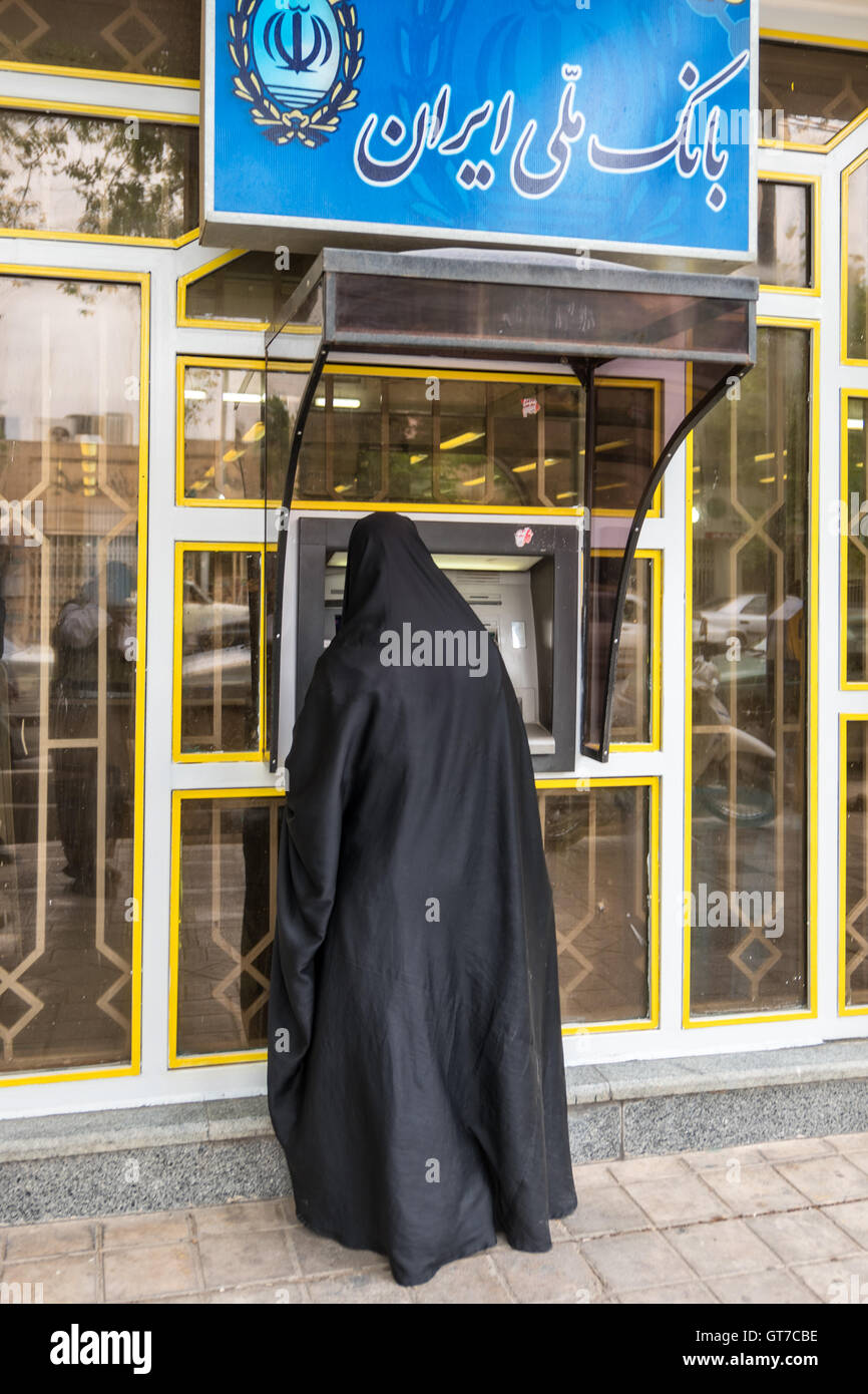 Woman wearing a chador uses an ATM machine at a bank to get cash in ...