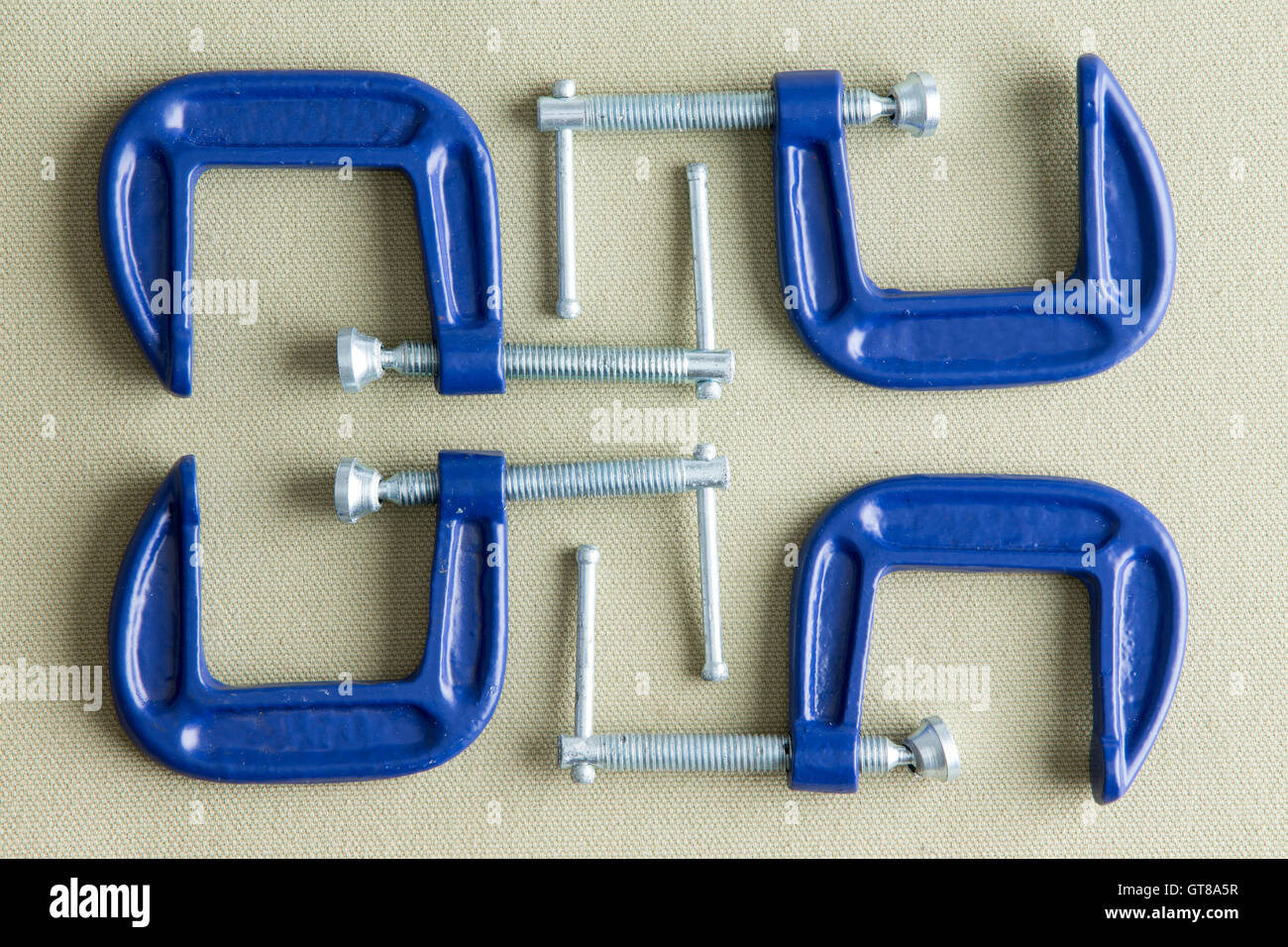 Four blue steel g-clamps neatly arranged on a grey background viewed ...