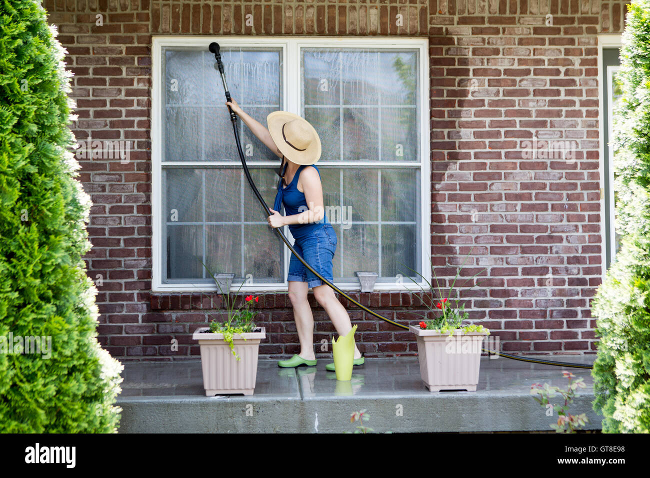 Housewife standing on a patio washing the windows of her house with a ...