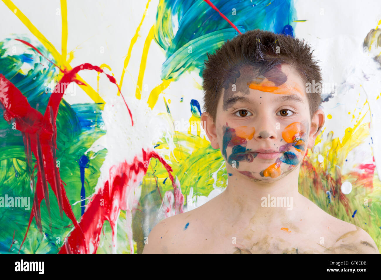 Young artist posing shirtless with his face covered in paint splodges ...