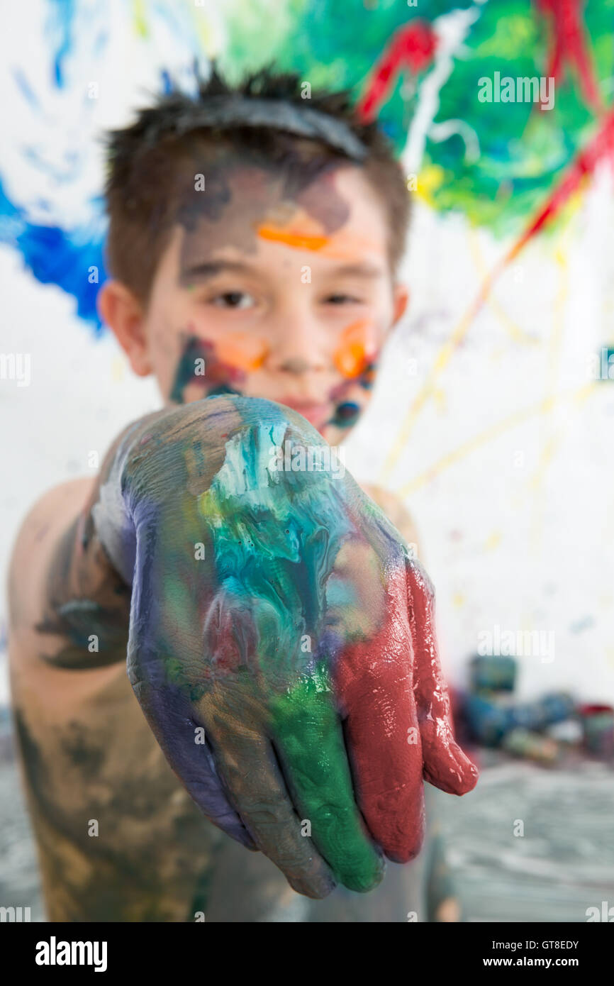 Artistic little boy holding out his paint covered hand to the camera as ...