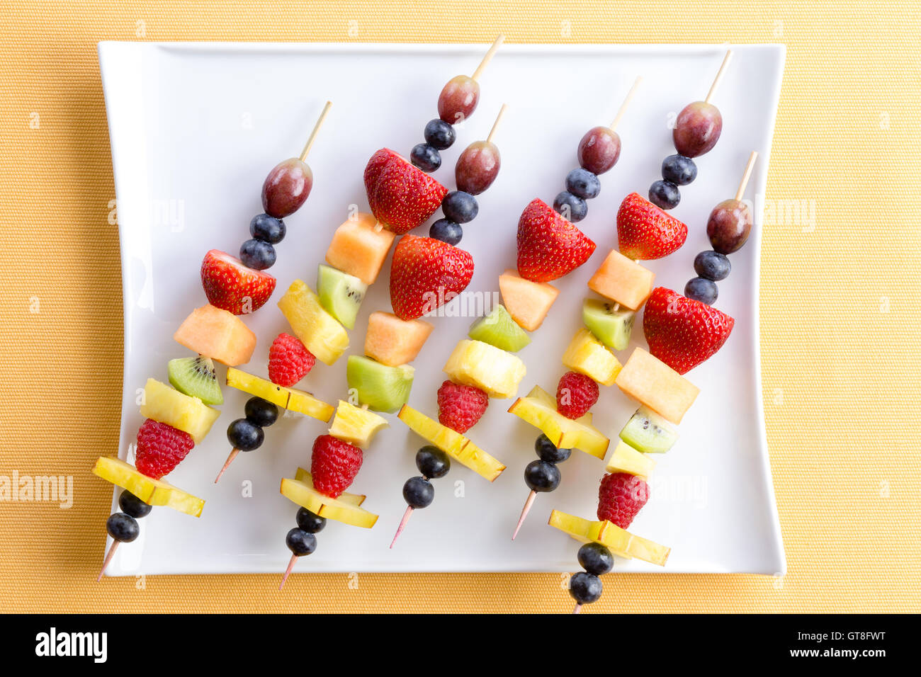 Fresh fruit shish kebabs arranged diagonally on a modern square plate ...
