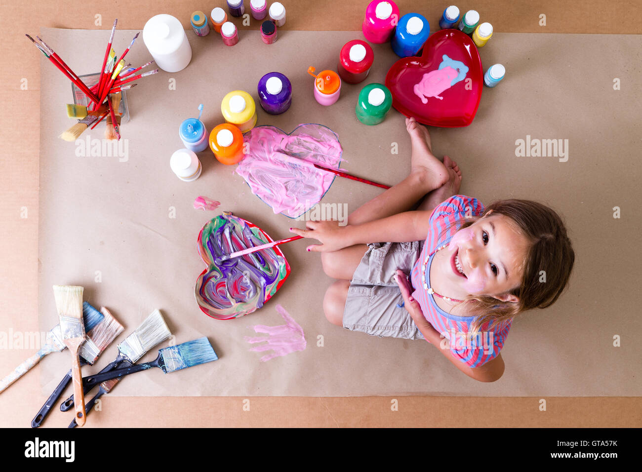 Pretty creative little girl artist kneeling on brown paper with her ...