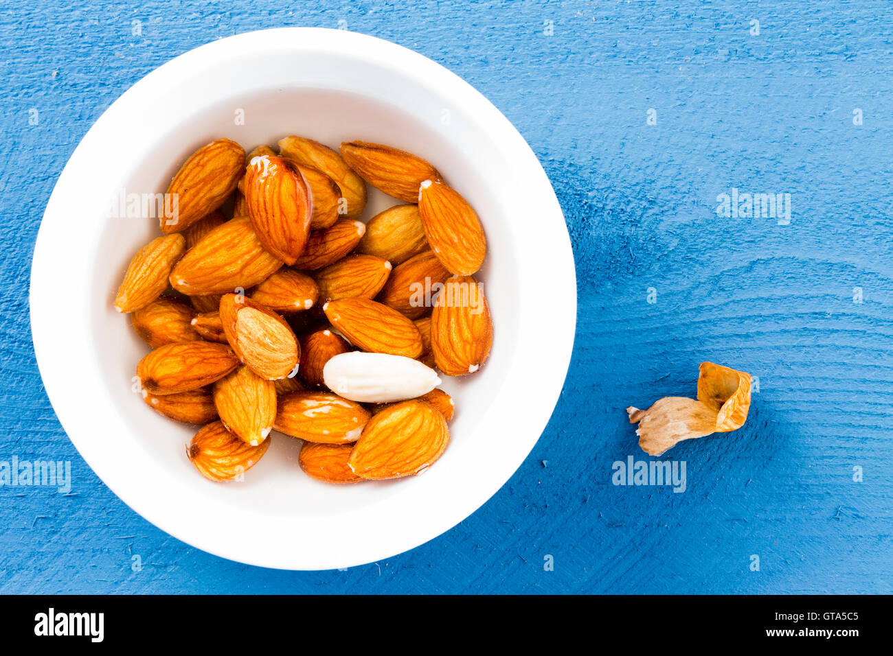 Bowl of fresh raw almonds with one peeled against a blue background as ...