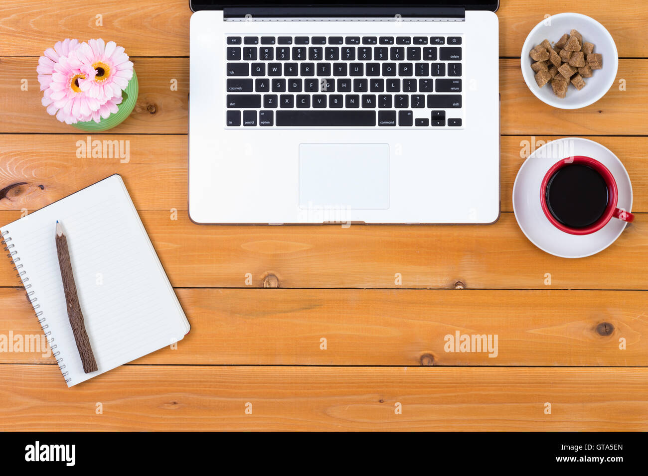 Neat clean wooden desk with laptop computer, notepad, flowers and a mug ...