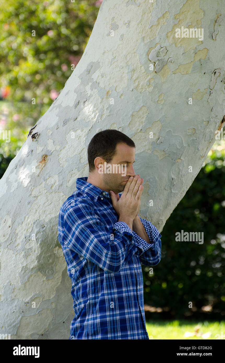 Stopping to pray in a park - Man praying next to a large tree trunk ...