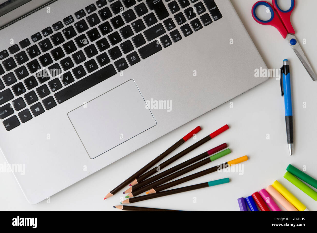 Laptop keyboard and some objects such as pen, colored pencils, felt tip ...