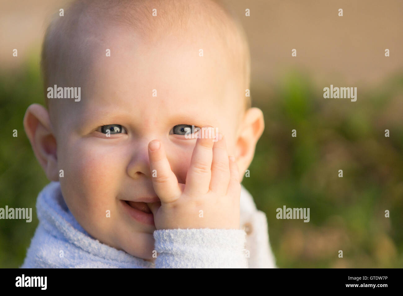 Cute happy smiling baby boy outdoors with thumb in mouth looking at ...