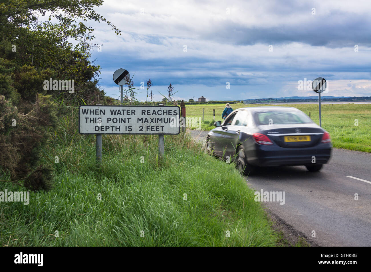 A car driving past a tidal flood warning sign on the road into Bowness ...