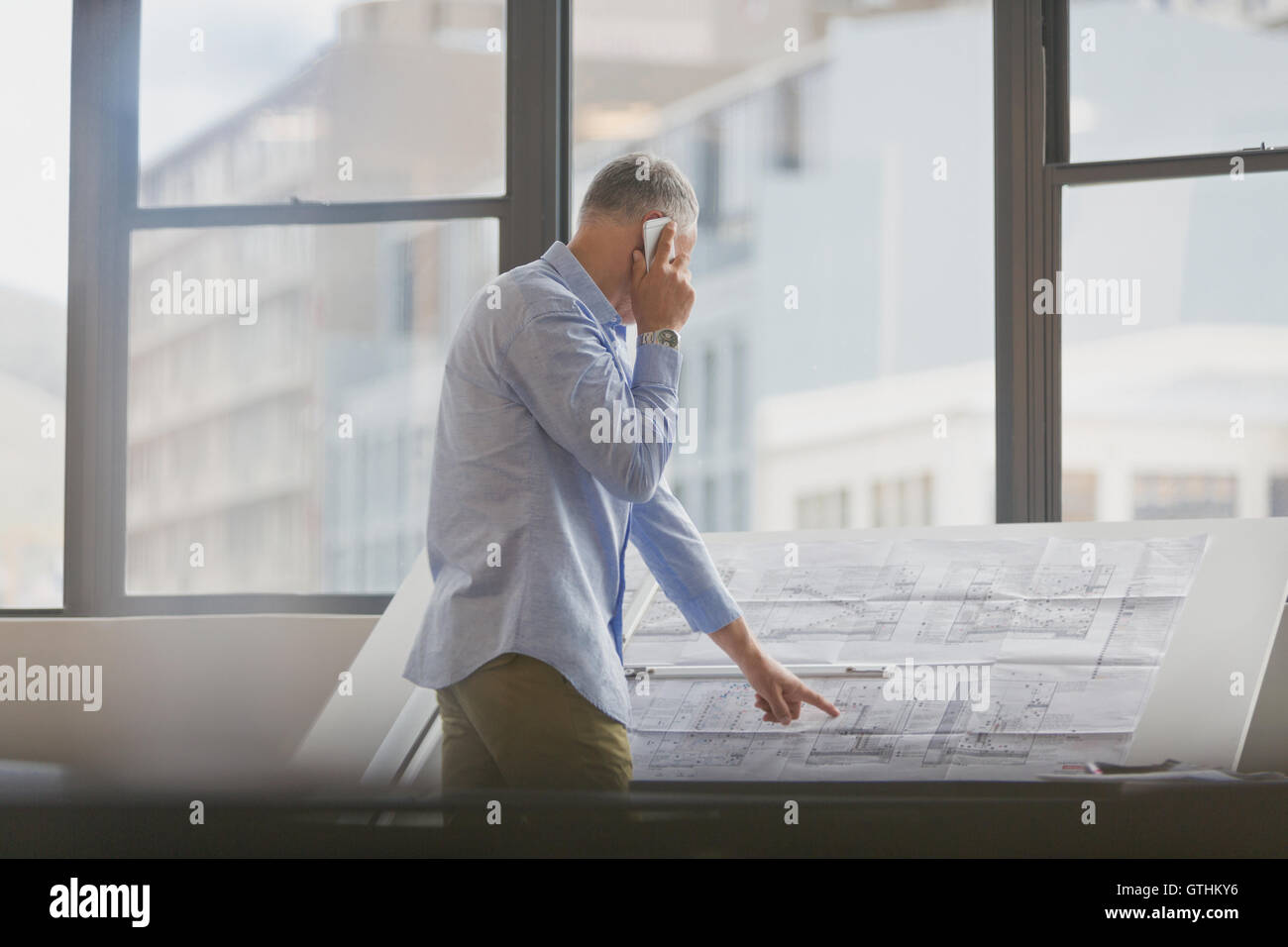 Architect talking on cell phone reviewing blueprints in office Stock ...
