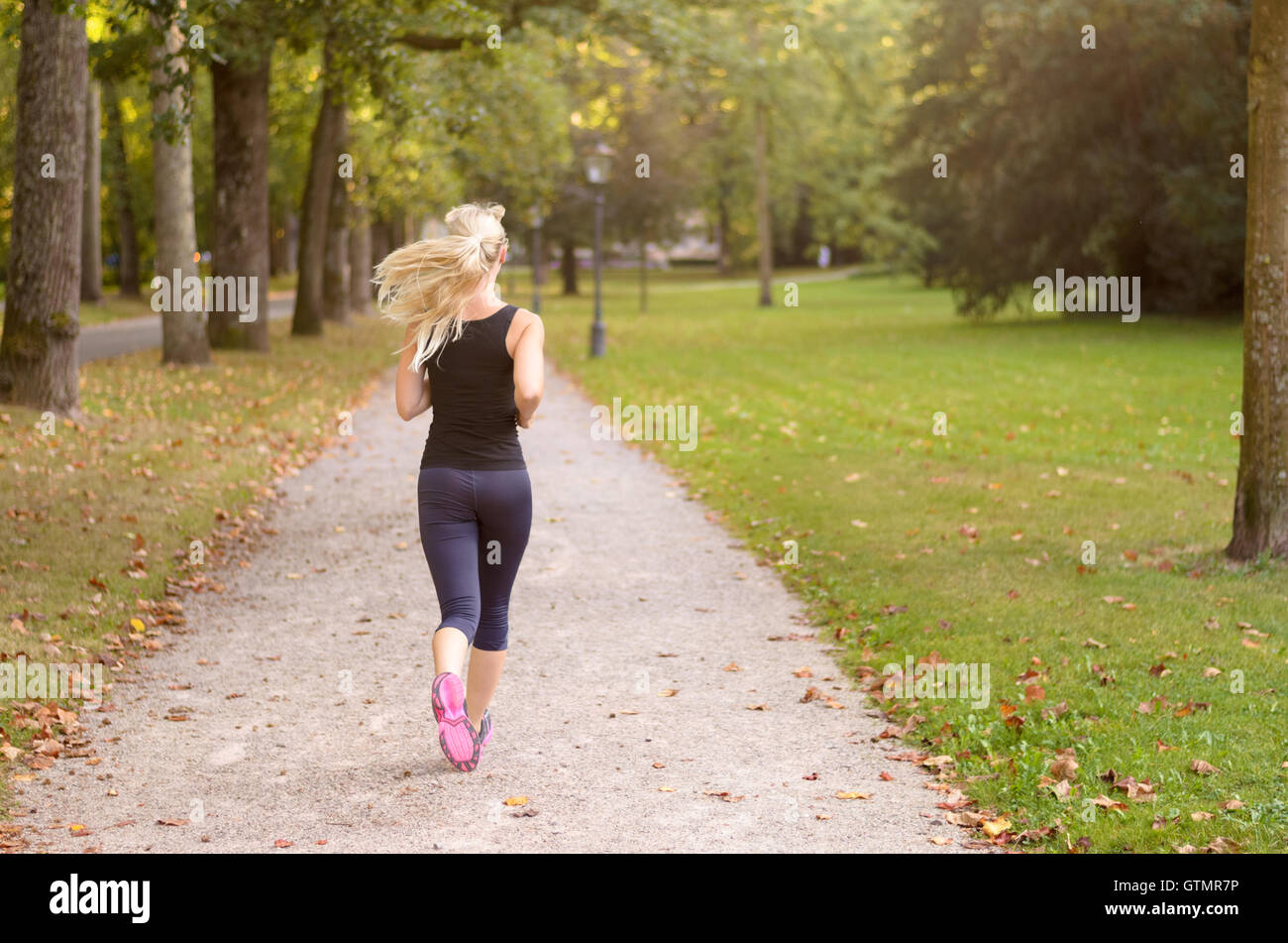 Fit active young woman jogging through a park away from the camera down ...