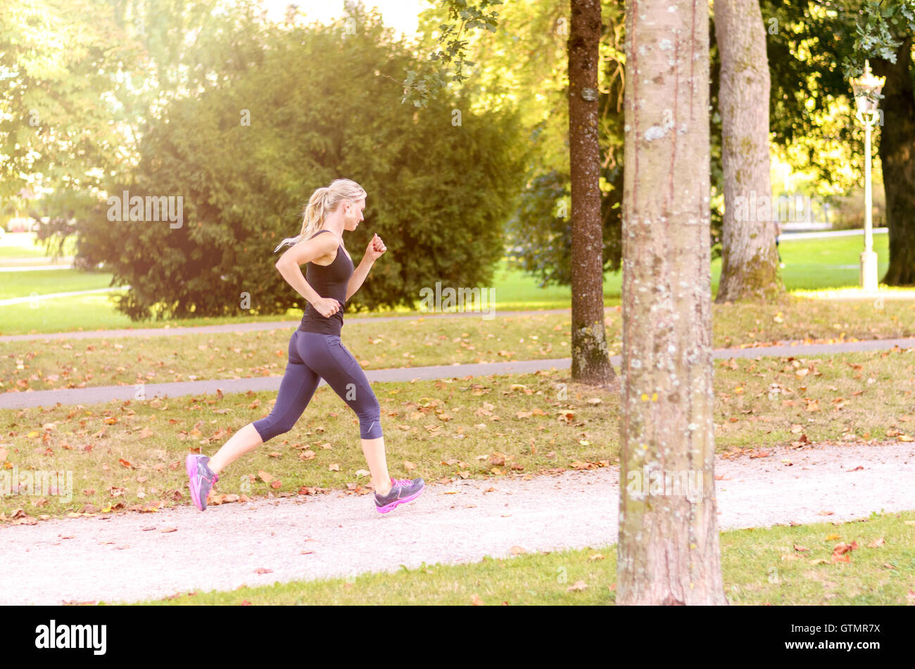 Fit active young woman jogging through a park running along a path ...