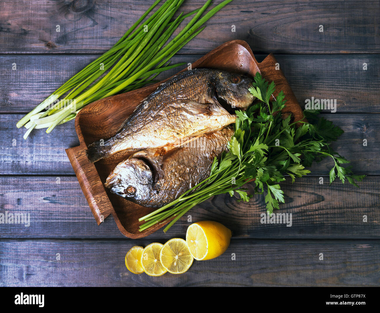 On a wooden table plate with two roasted carp fish dorado with parsley ...