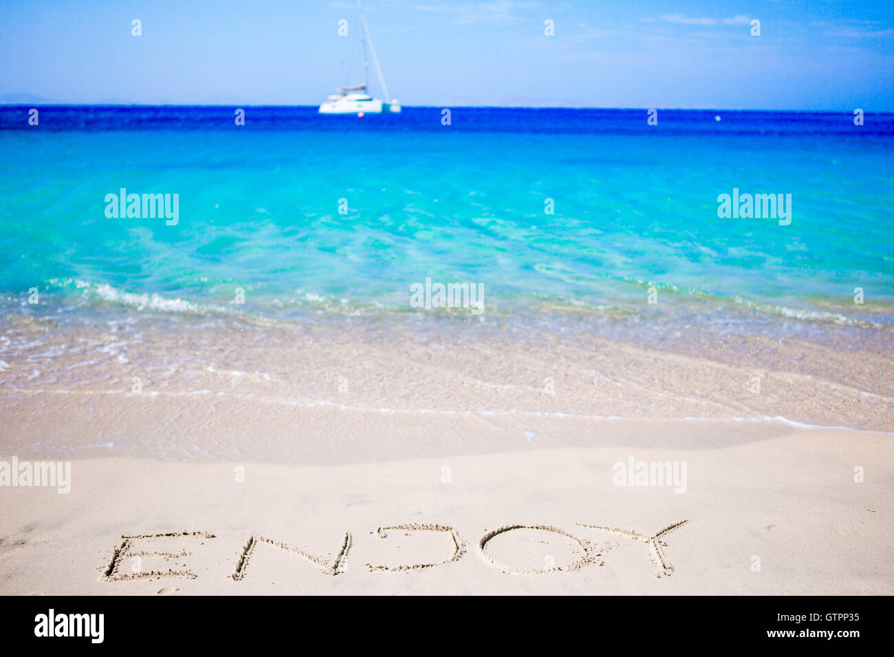 Word Enjoy handwritten on sandy beach with soft ocean wave on ...