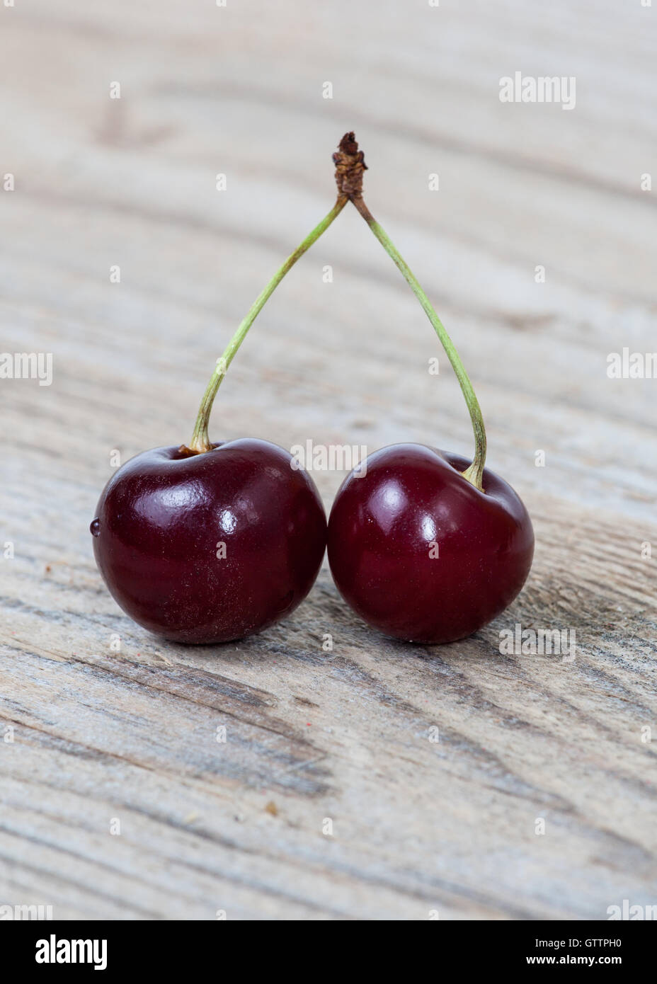 Two red cherry berries with joined stalks on a wooden board. Closeup ...