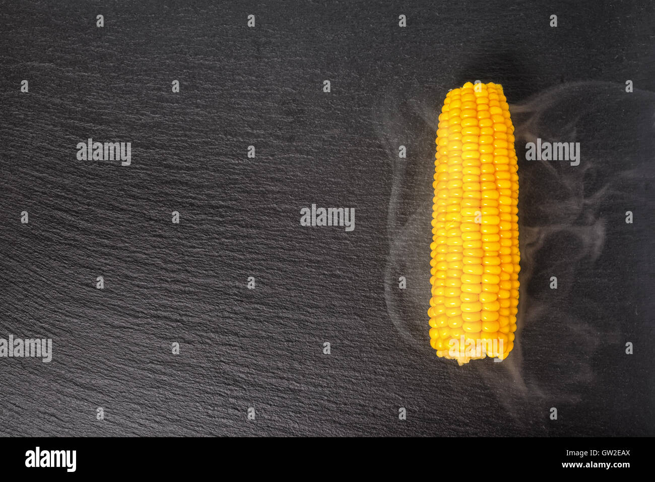 cooked yellow corn with steam served over black slate stone background ...
