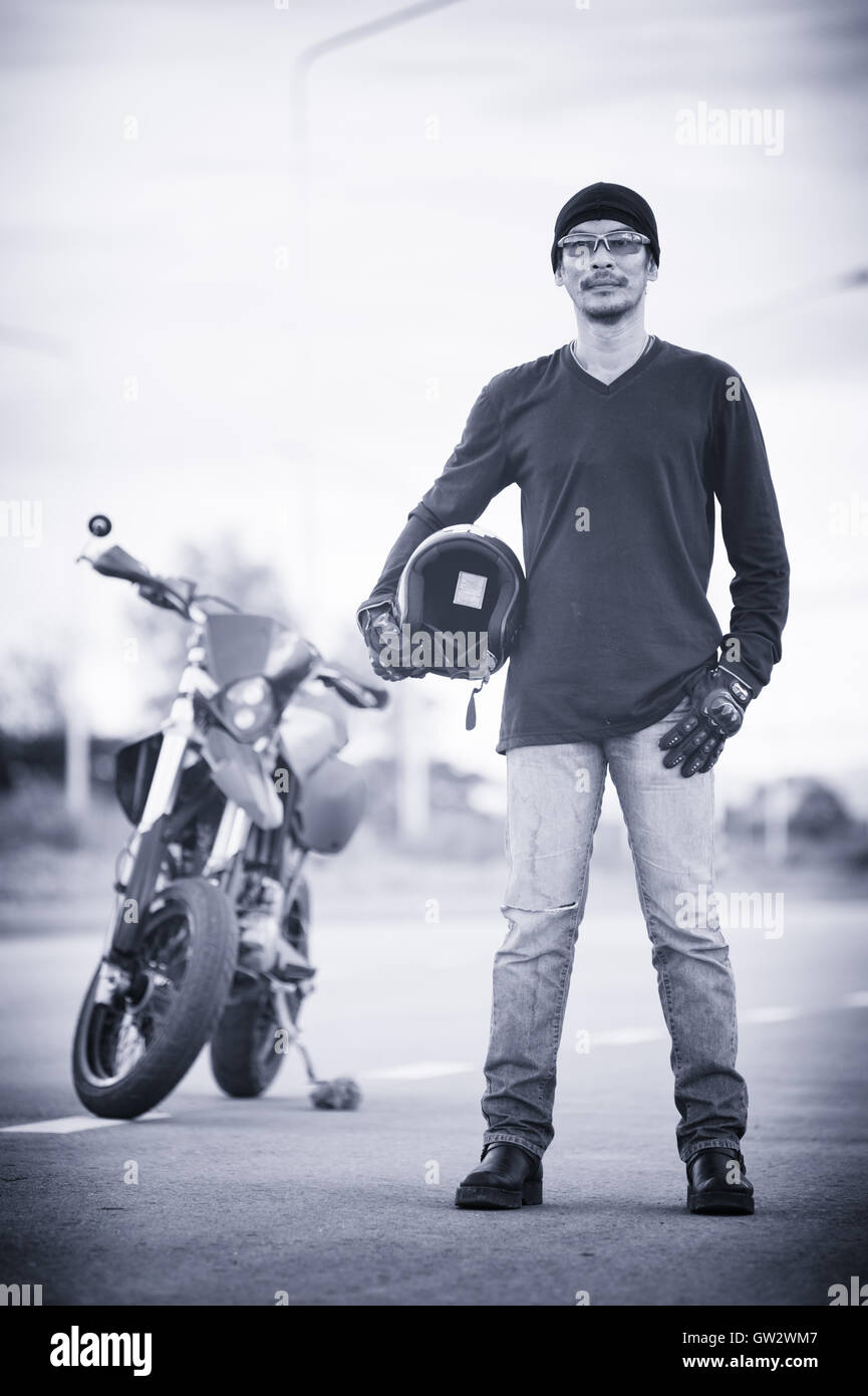 portrait of man biker standing on road with motorcycle in sunset ...