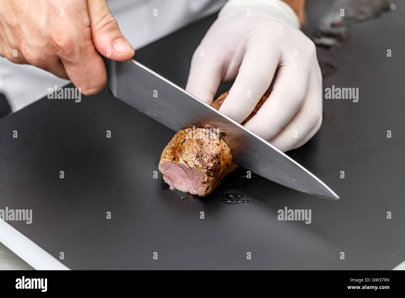 Chef in restaurant kitchen cooking, he is cutting loin pork meat Stock ...