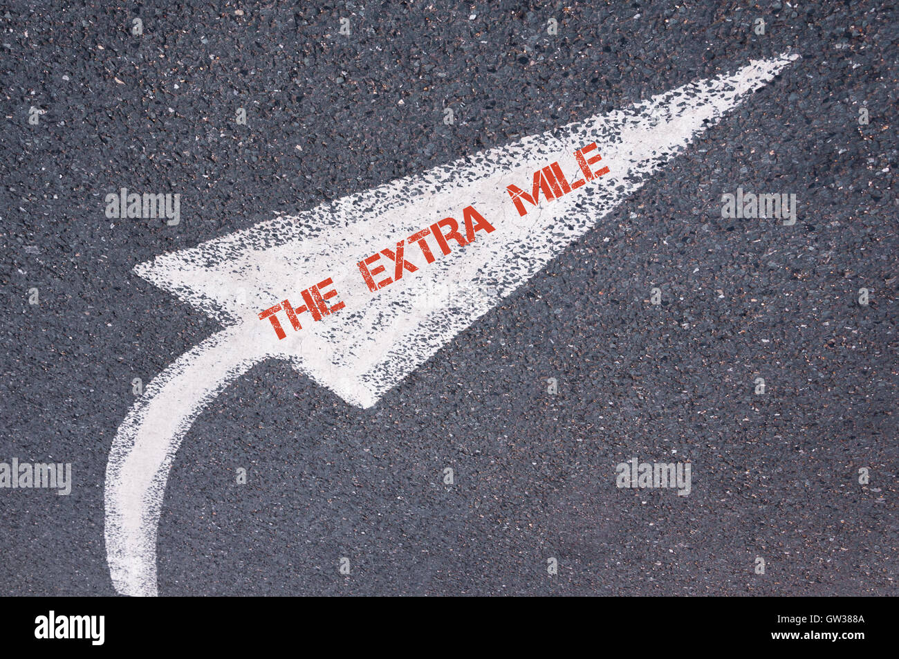 Directional white painted arrow with words THE EXTRA MILE over road ...