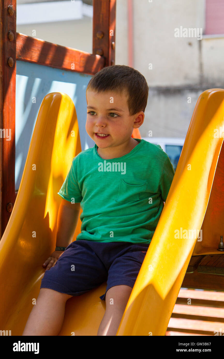 Adorable little boy playing on a slide in a kids outdoor playground ...
