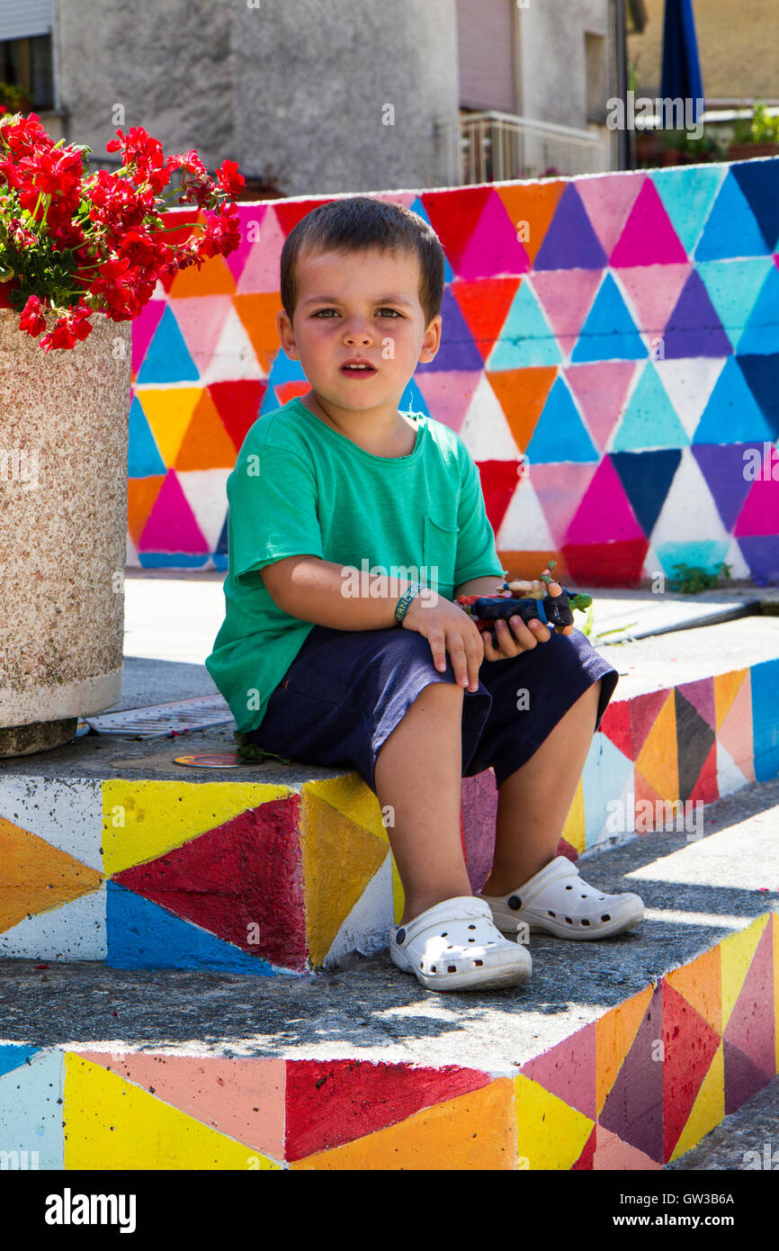 portrait of little boy sitting on the steps and colorful wall ...