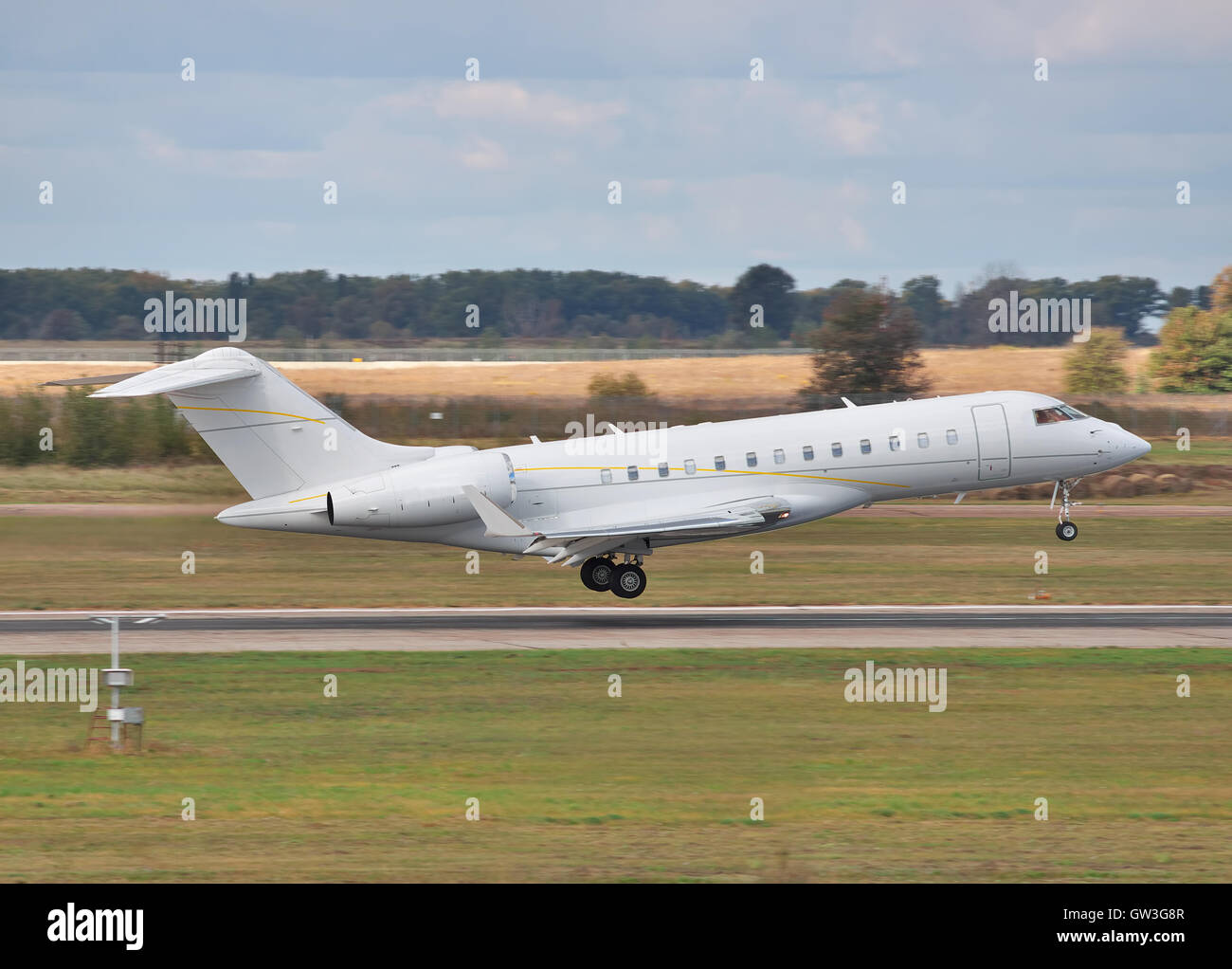 Business jet is landing on the runway with cloudy sky on the background ...