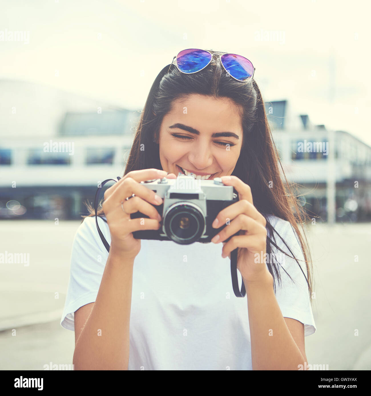 Laughing young woman checking the viewfinder on the back of her camera ...