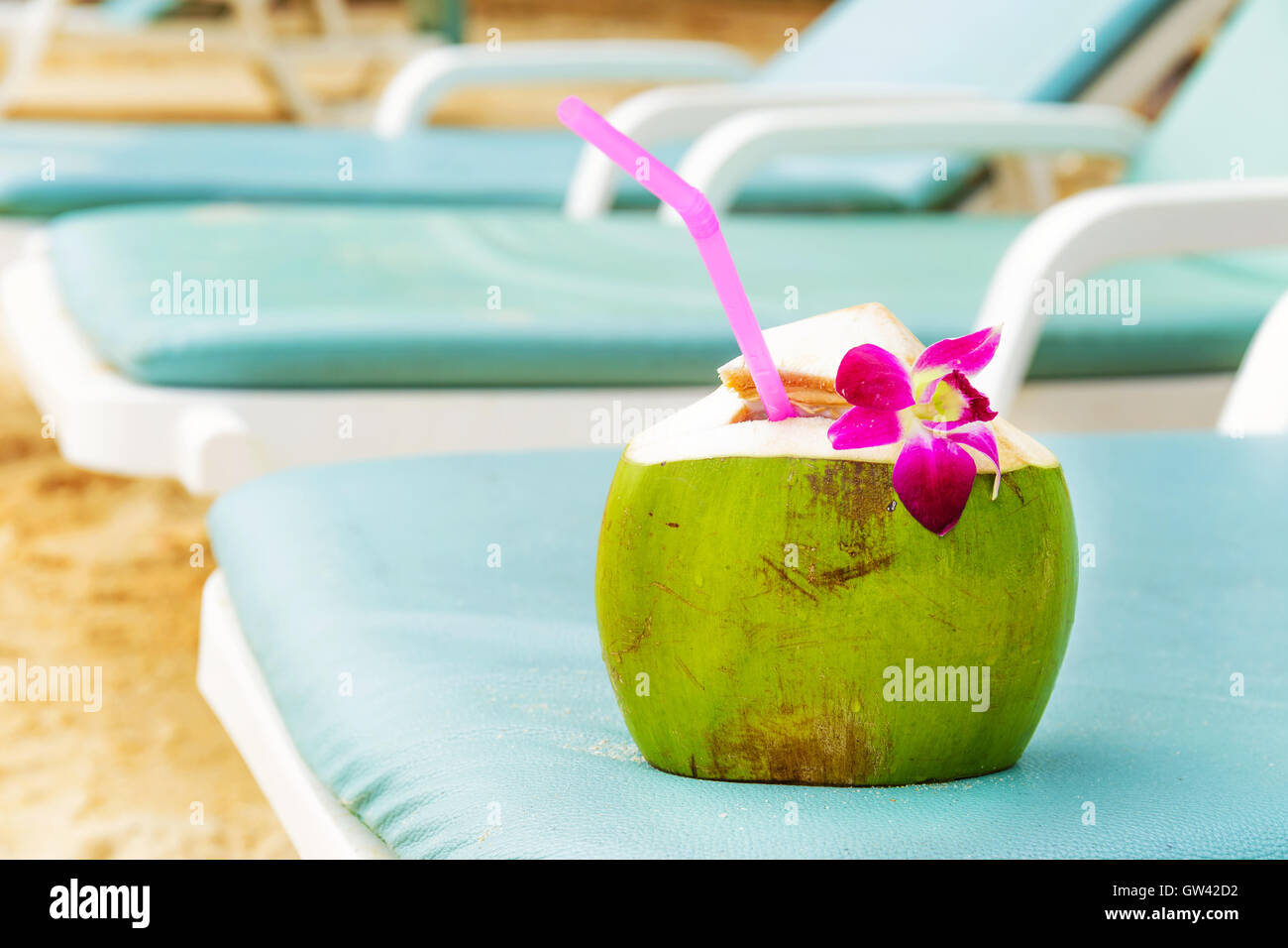 Coconut with drinking straw on beach bench Stock Photo - Alamy