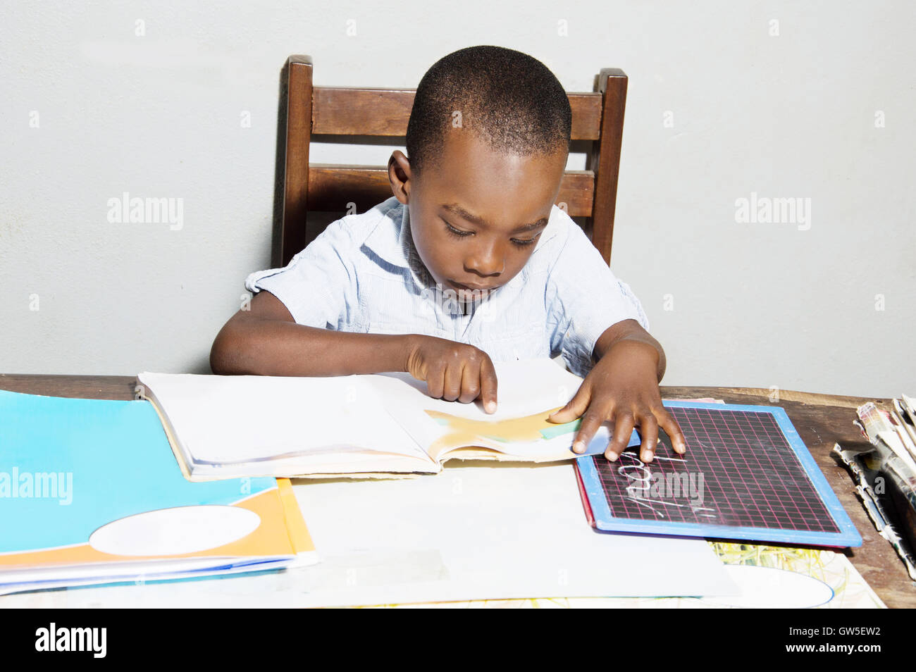 child is studying at home with his reading book, his slate and his ...