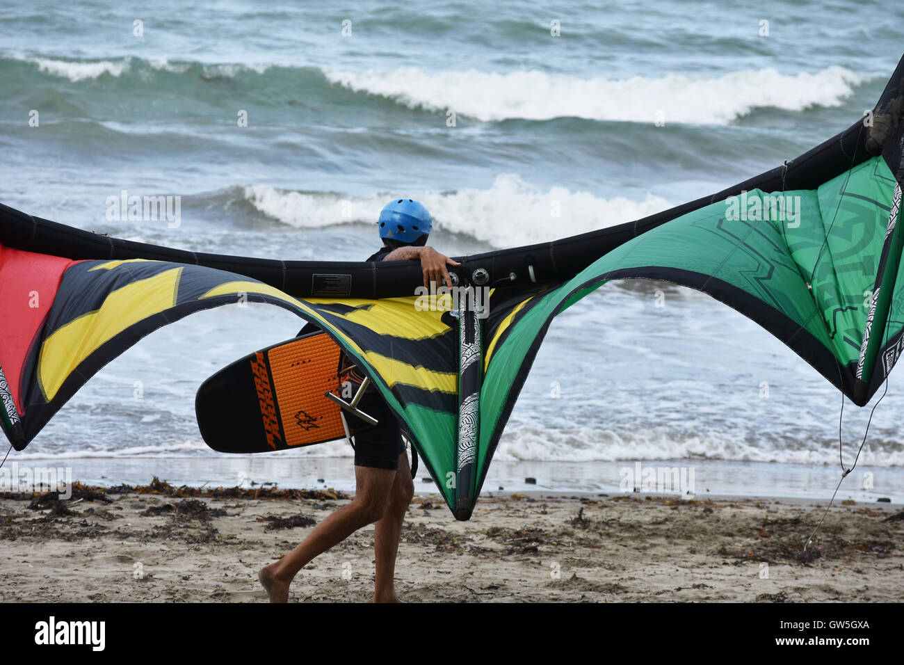 Kitesurfer wearing helmet carrying colourful kite on beach Stock Photo ...