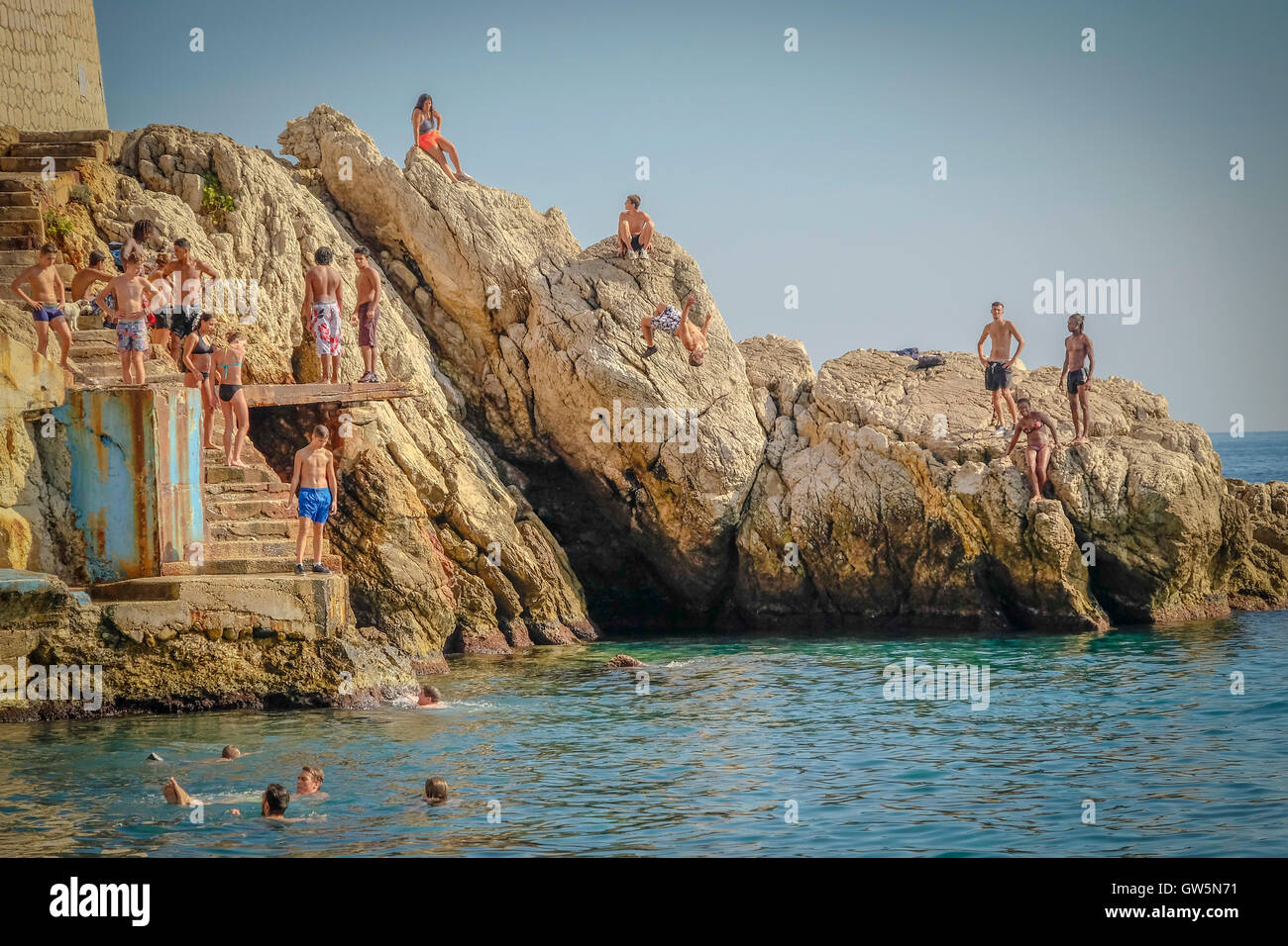 Young boys dive off a platform into the blue waters of the ...