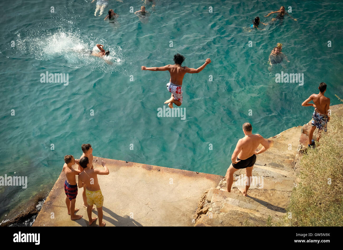 Young boys dive off a platform into the blue waters of the ...