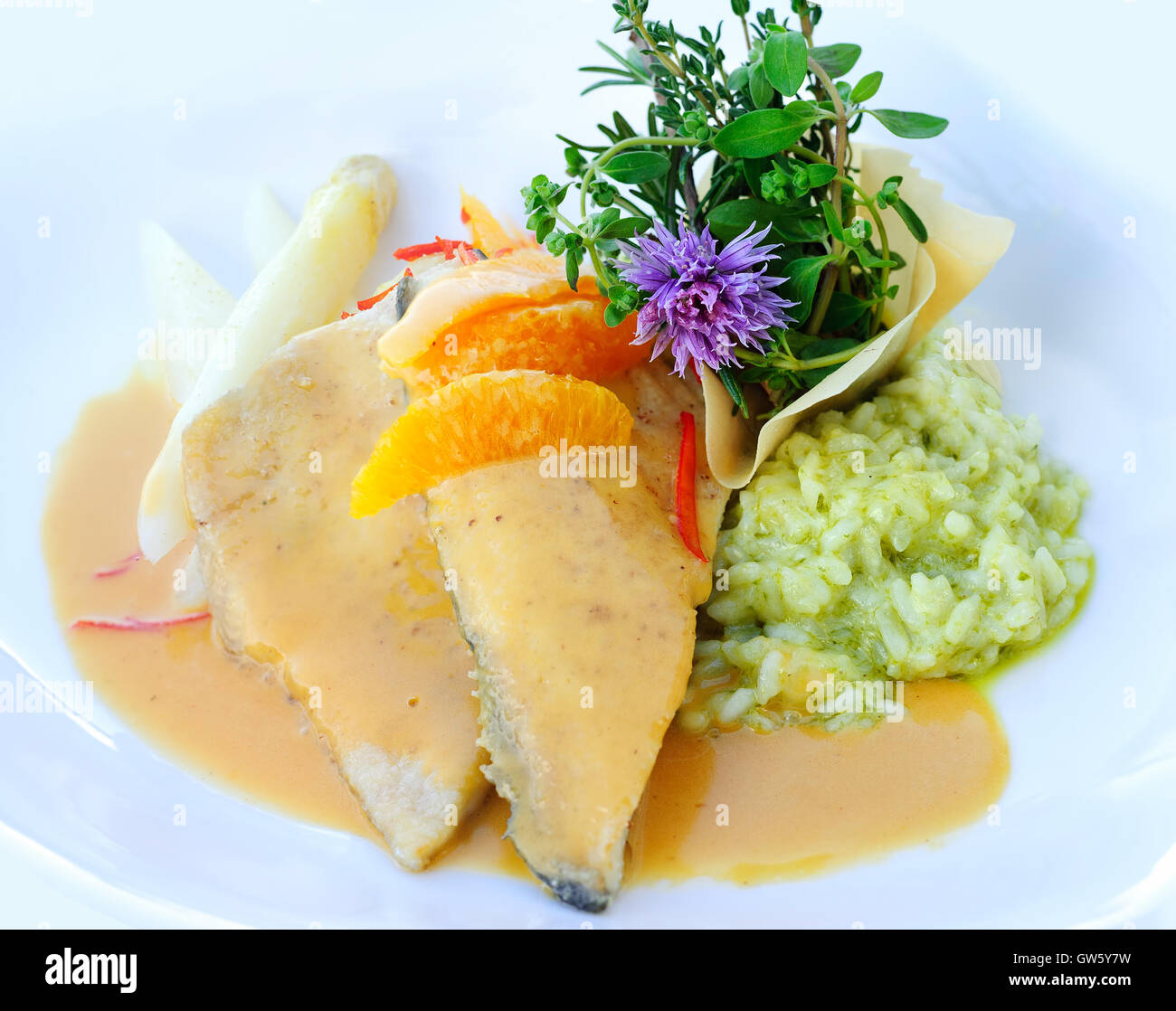 Fried fish with green risotto and orange sauce, decorated with fresh ...