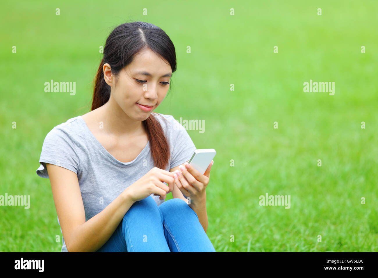 Woman sitting on grass with smartphone Stock Photo - Alamy