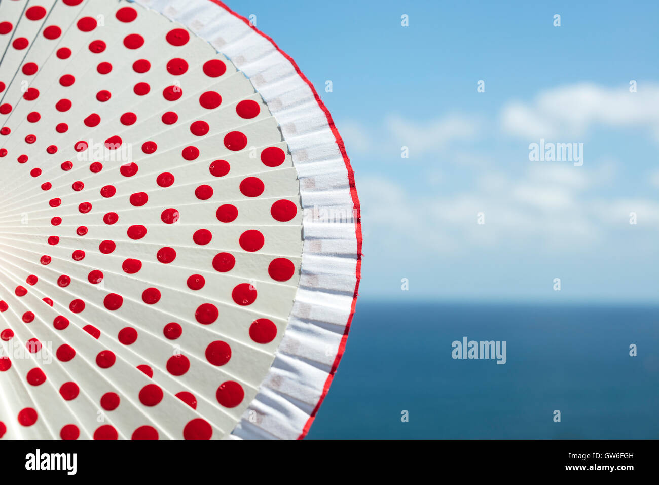 White Hand-held fan (or spanish fan) with red dots and the sea at the ...