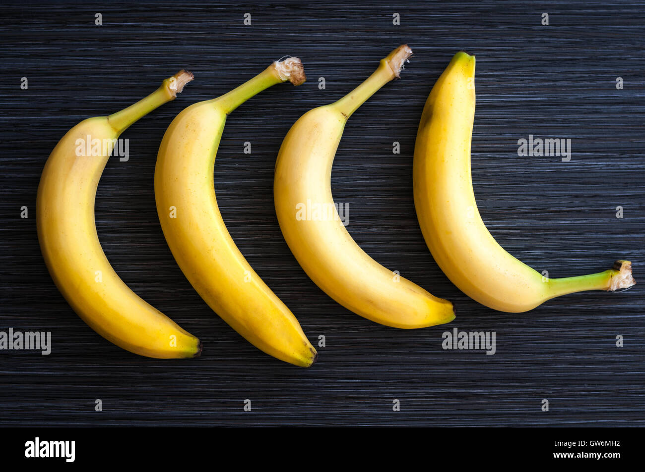 four ripe bananas laid out in a row on dark background close-up Stock ...