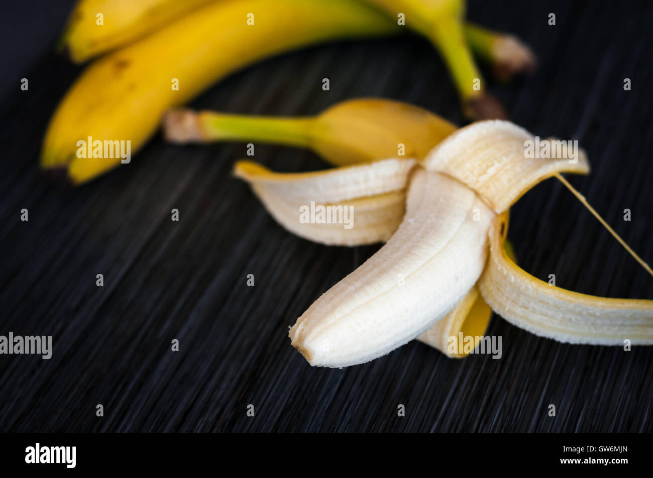 three ripe bananas, one peeled half on a dark background close-up Stock ...