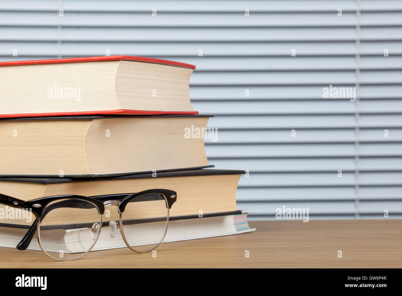Stack of rerading books on a table with a pair of black rimmed eye ...