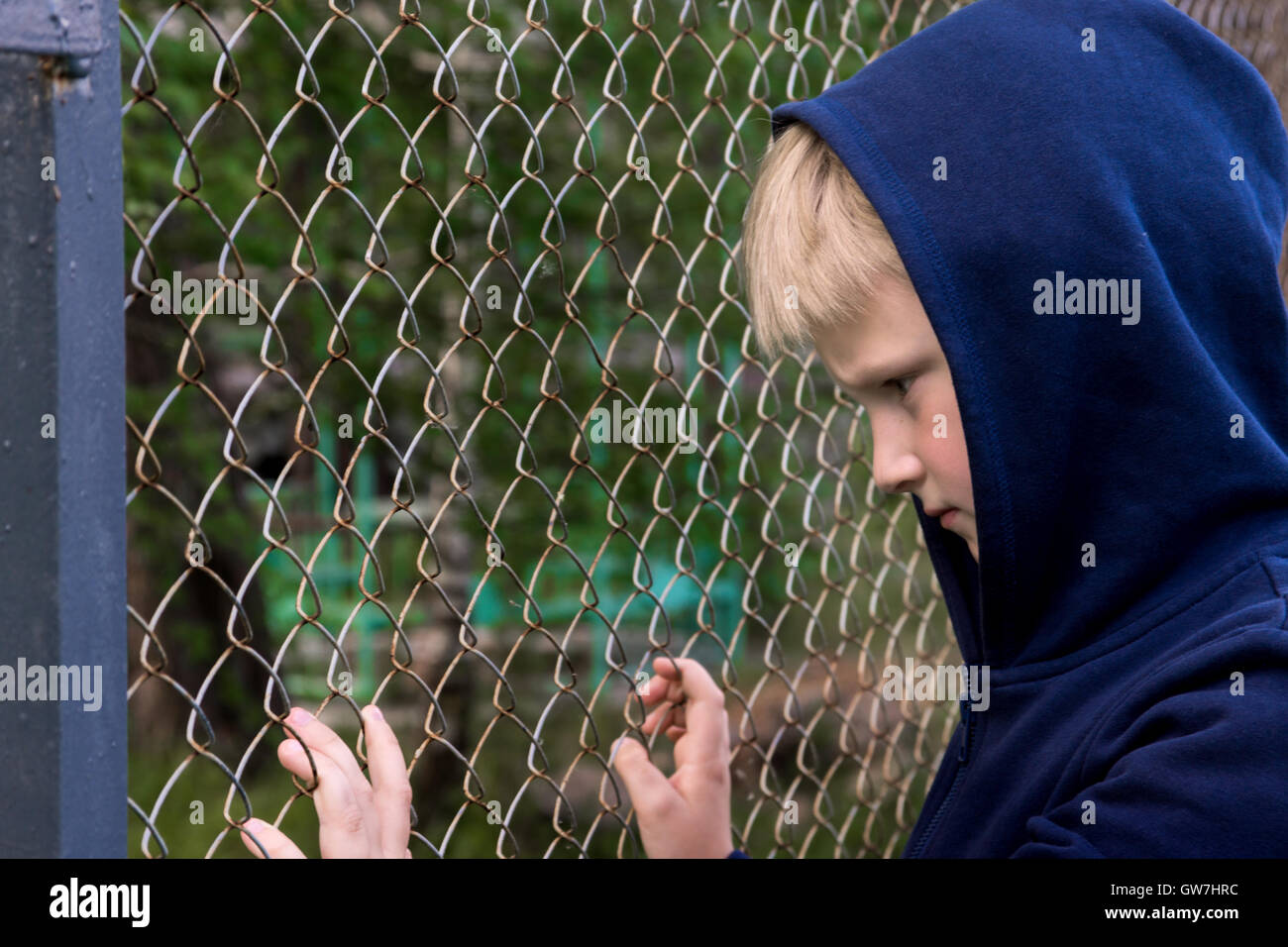 Depressed, frustrated boy (child, kid, teen) near metal mesh, close up ...