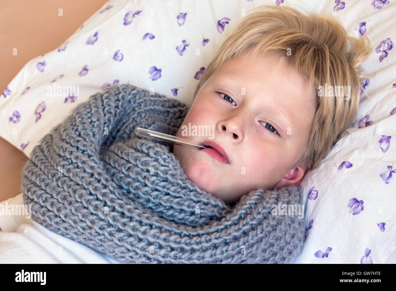 Sick little boy holding thermometer laying in bed with sad face ...