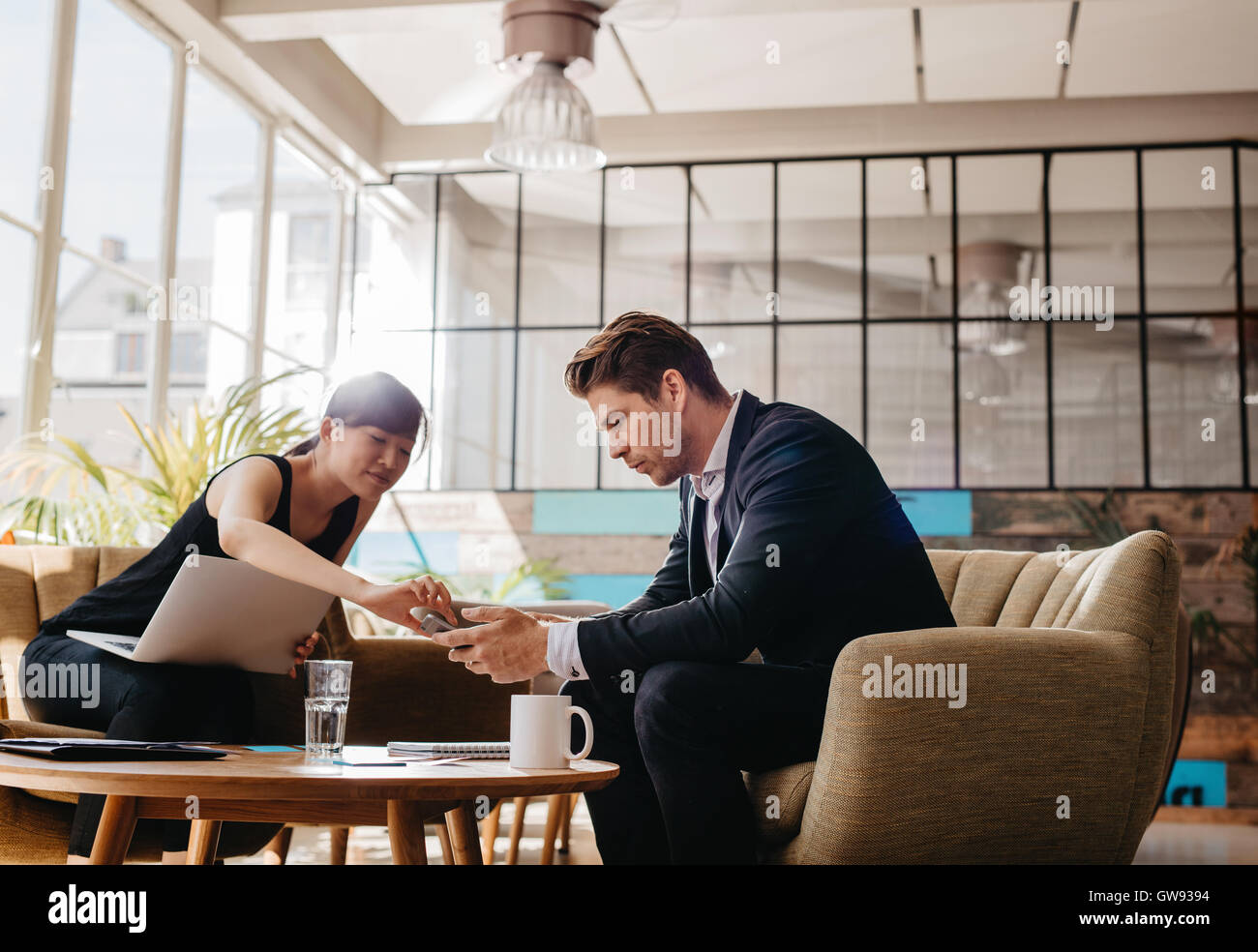 Shot of two people sitting in office lobby. Business partners working ...