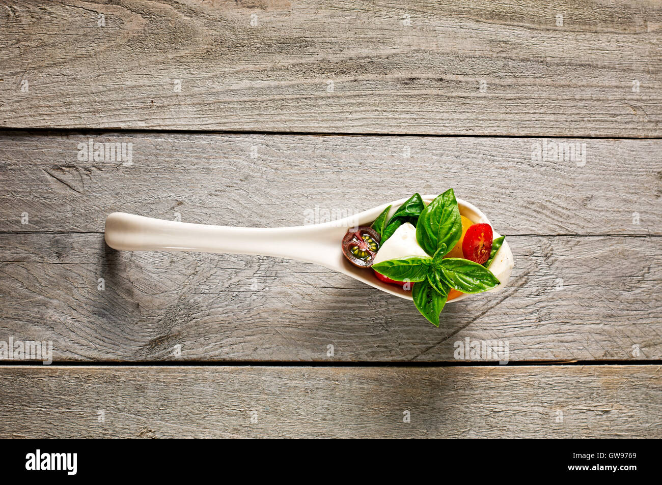 Fresh farm style caprese salad in a porcelain spoon on a weathered ...