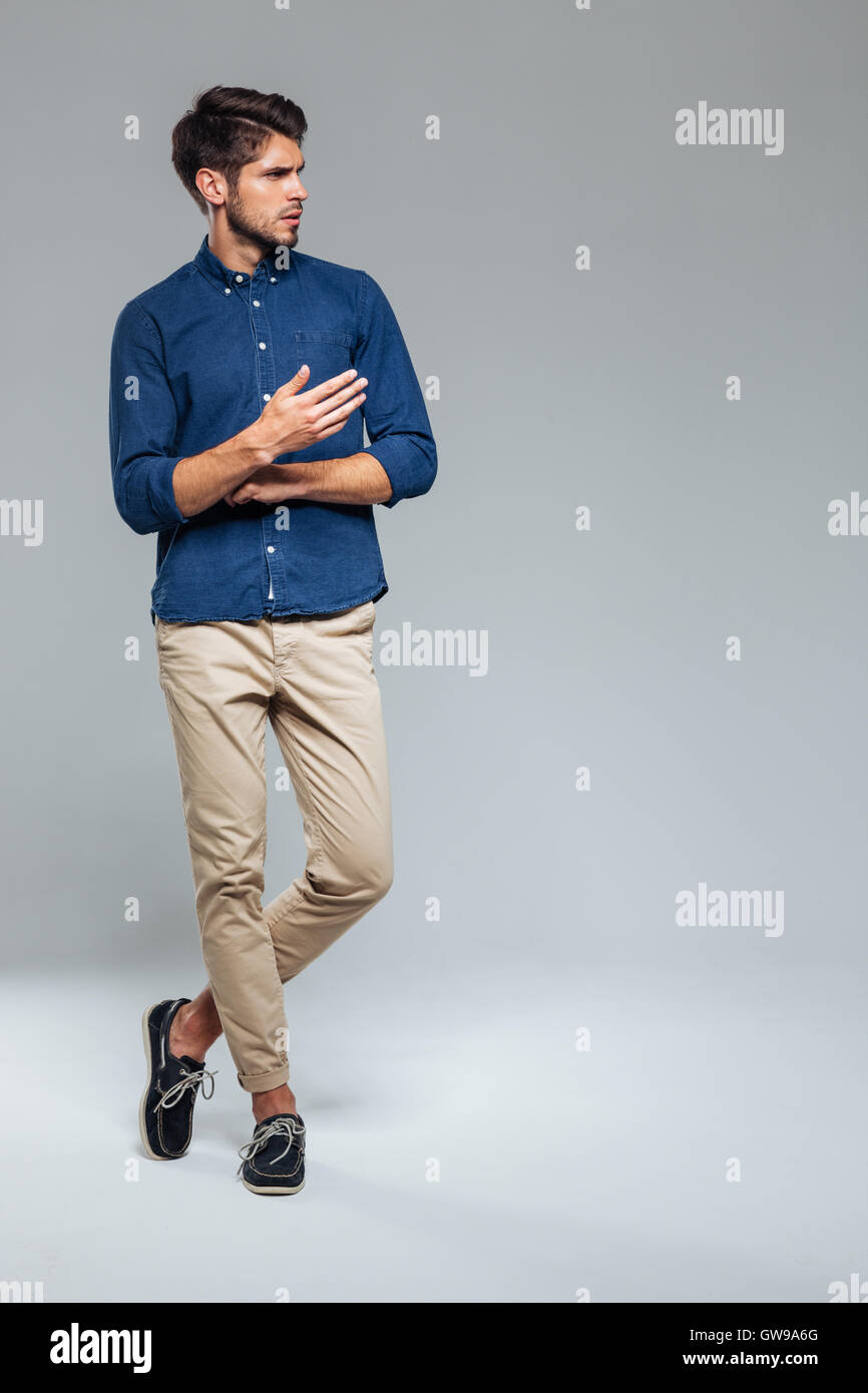 Full length portrait of a casual man standing with legs crossed over ...